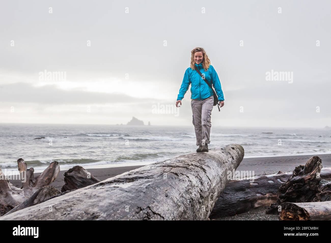 A woman walking on a large driftwood log above a beach. Rialto Beach ...