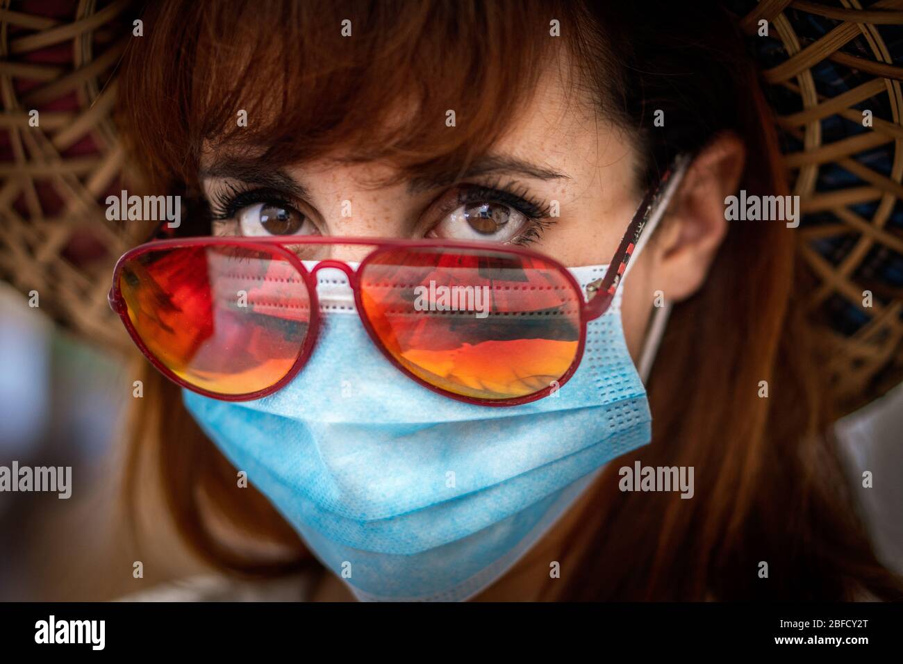 The new normal. A young woman wearing a surgical mask, red sunglasses ...