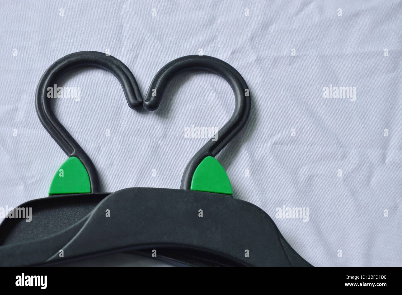 black plastic clothes hanger arranging heart shape on white fabric ...
