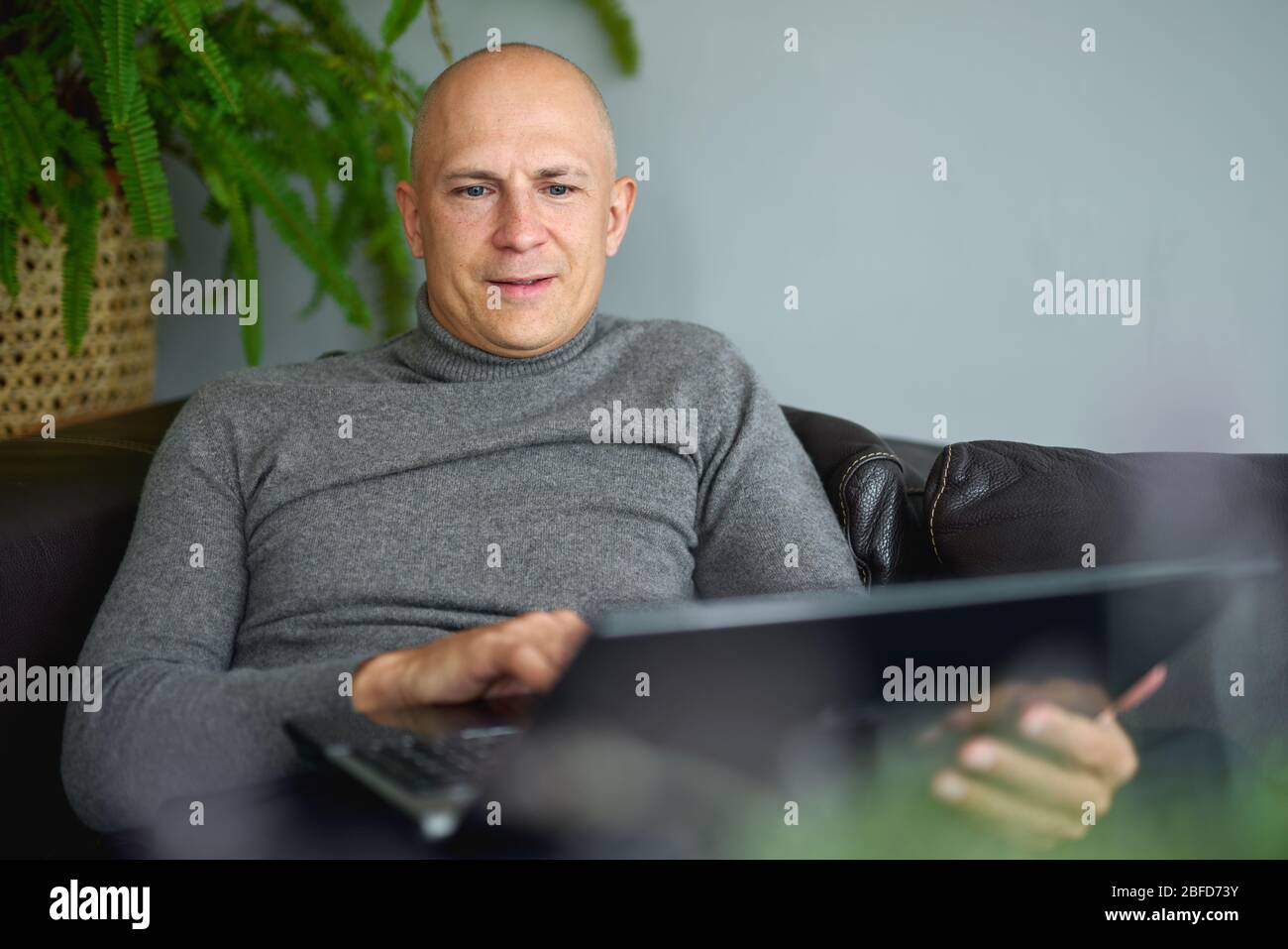 Handsome man working with notebook while sitting on the couch at home ...