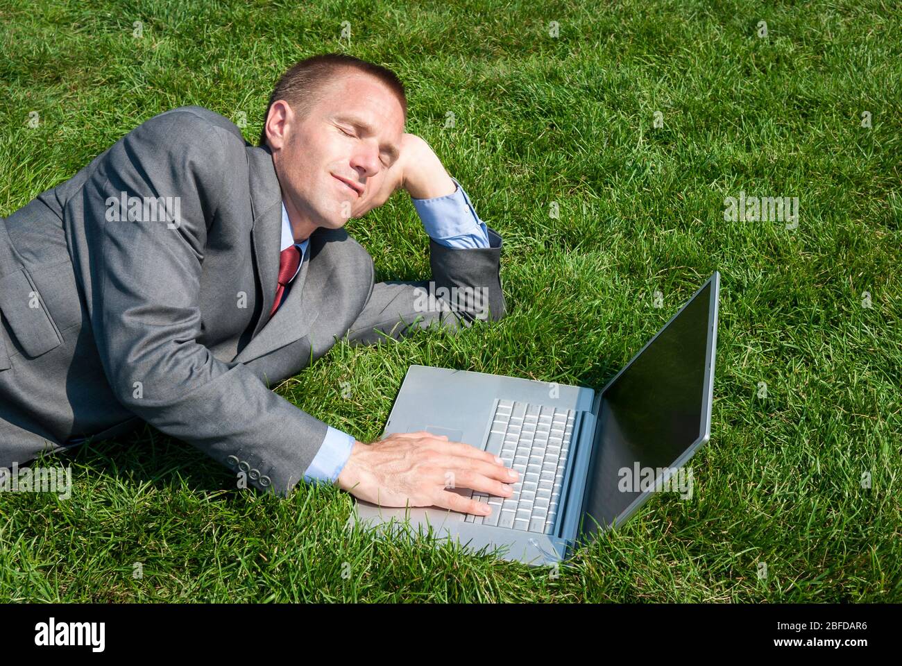 Lazy businessman relaxing on a sunny patch of green summer grass ...
