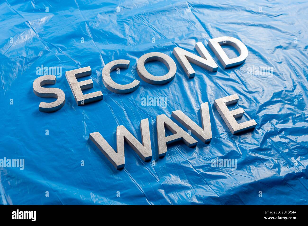 the words second wave laid with silver metal letters over crumpled blue ...