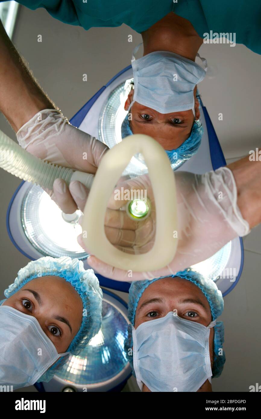 An anaesthetist holds a breathing mask underneath the operating lights ...