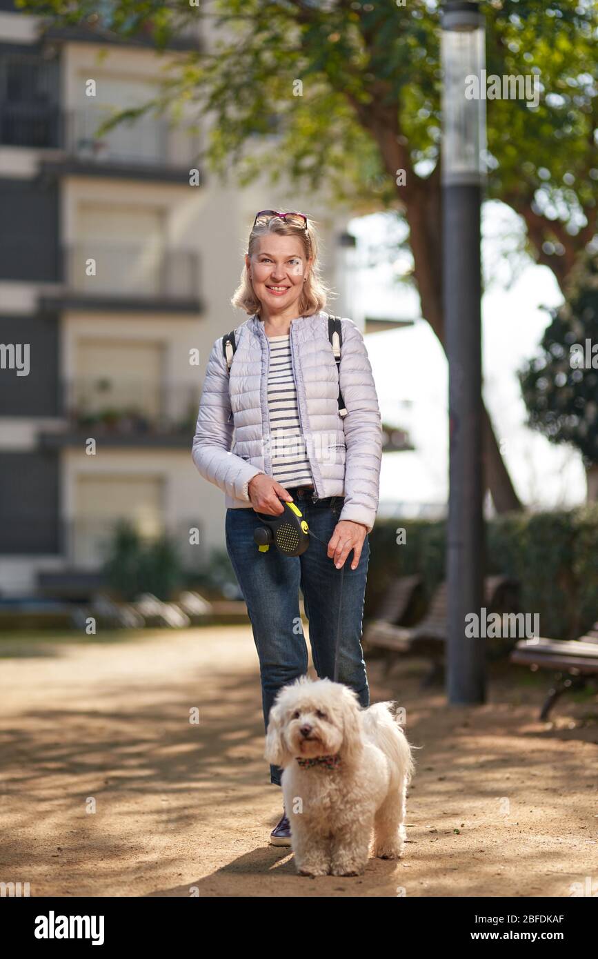 Attractive middle-aged blond woman walking with dog in summer city ...