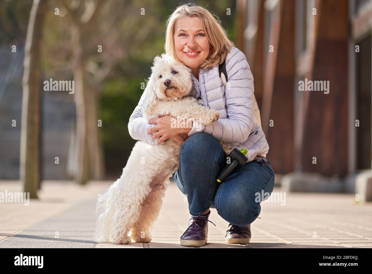 Mature woman walking with fluffy white dog in summer city Stock Photo ...