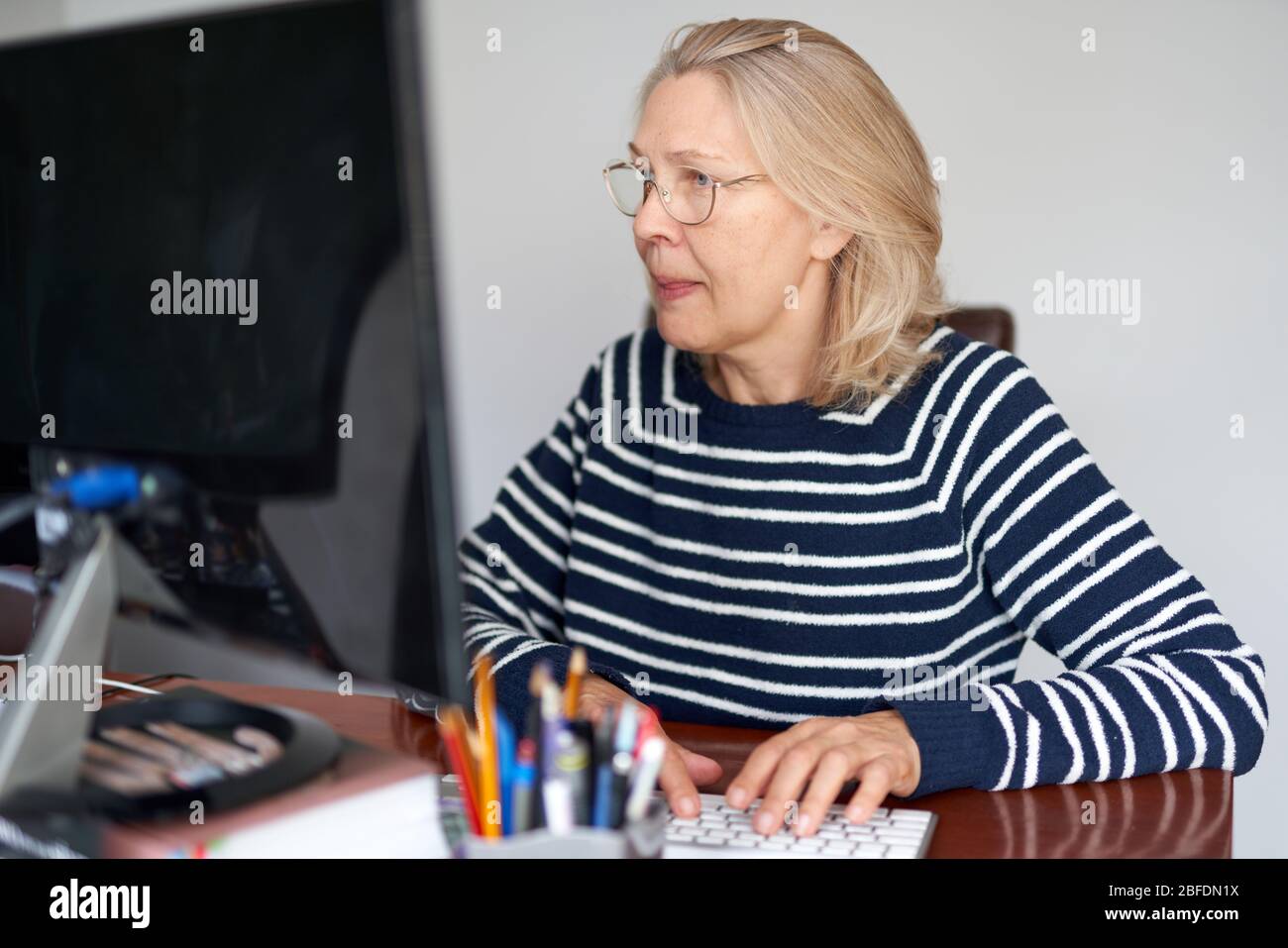 mature middle aged in glasses using laptop typing email working at home ...