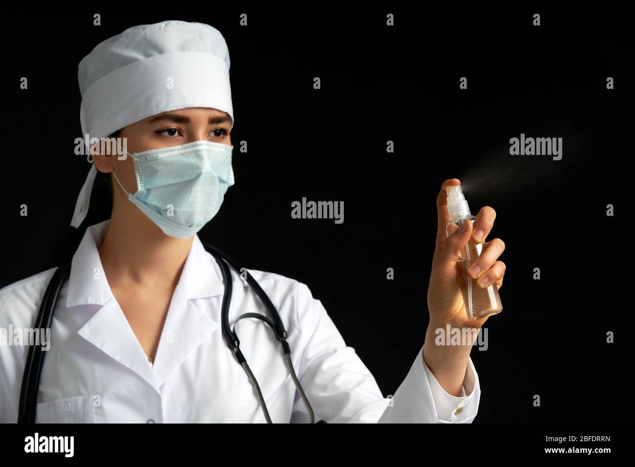 Young female doctor using spray antiseptic spray over black background ...