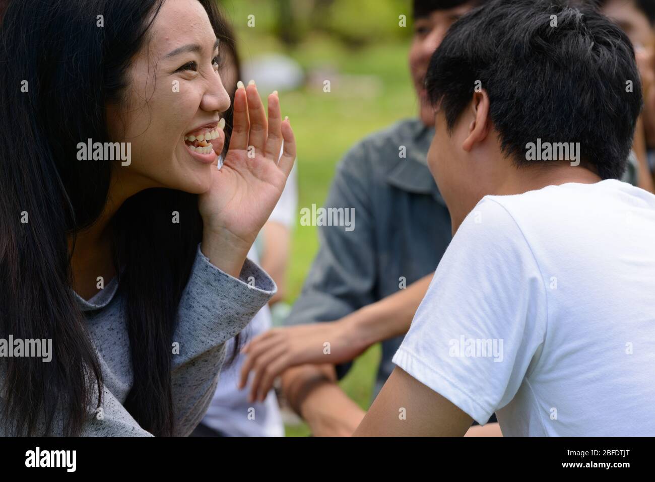 Two young Asian friends whispering together at the park Stock Photo - Alamy