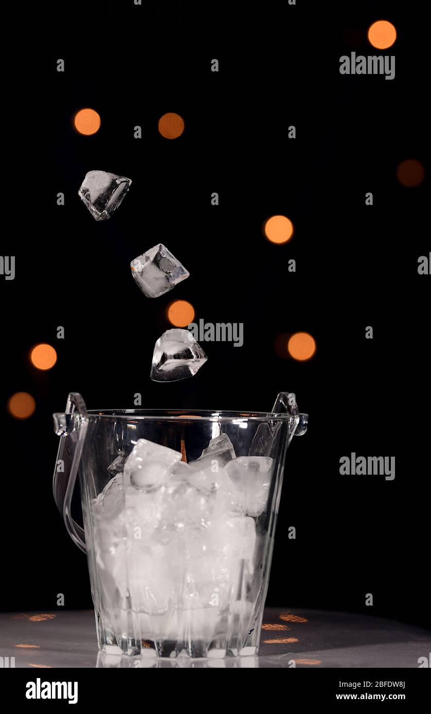 Dropping ice cubes inside ice bucket and photographed against beautiful light bokeh and isolated ...