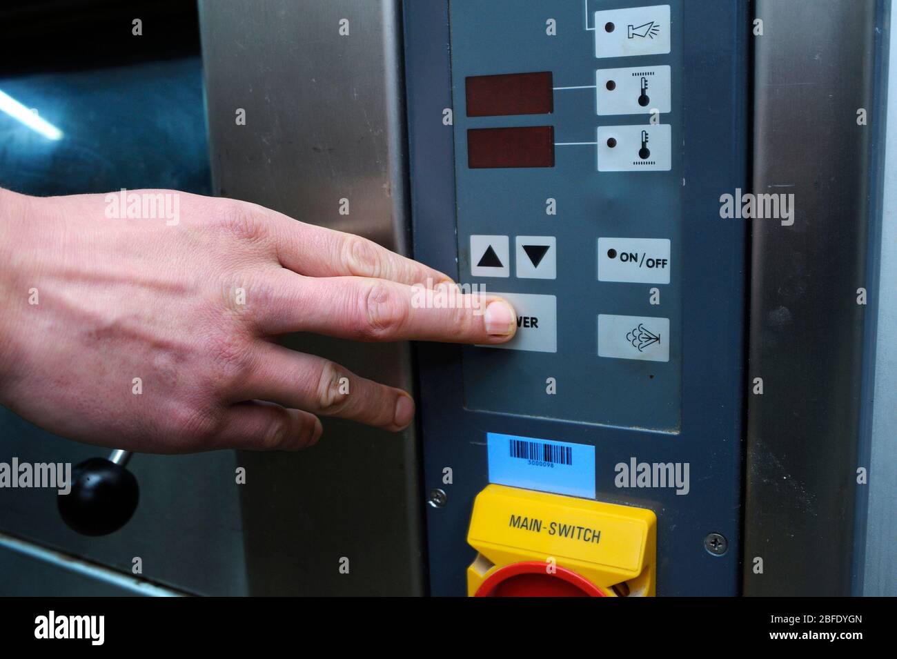 Baker hand pushing a power button on a control panel of an electric ...