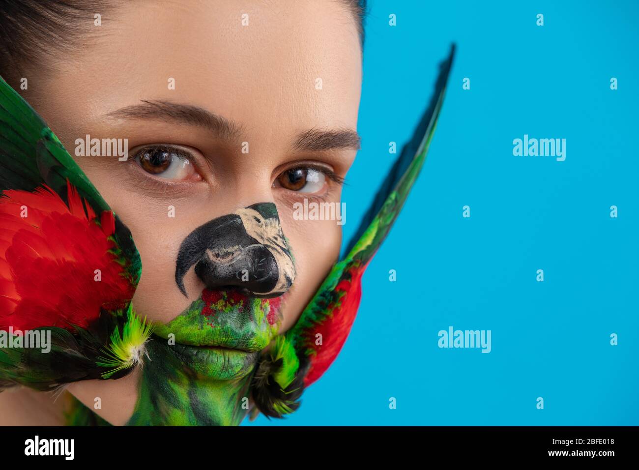 Woman with painted parrot bird on her face. Body art with real wings on ...