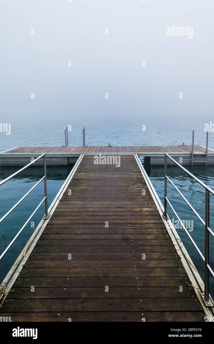 Wooden landing with swimming ladder leading the view onto a foggy blue ...