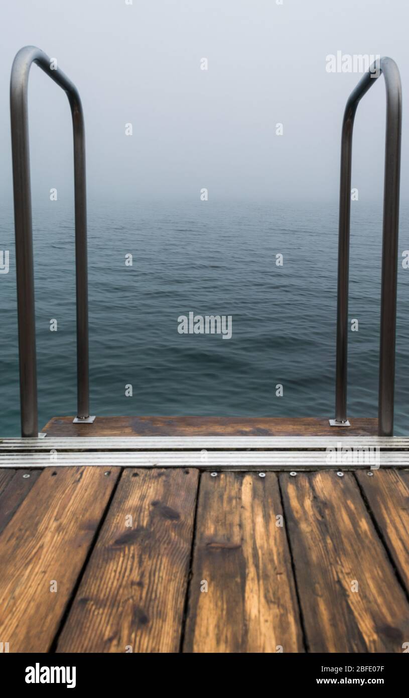 Swimming ladder at a landing with a view onto a foggy blue lake scenery ...