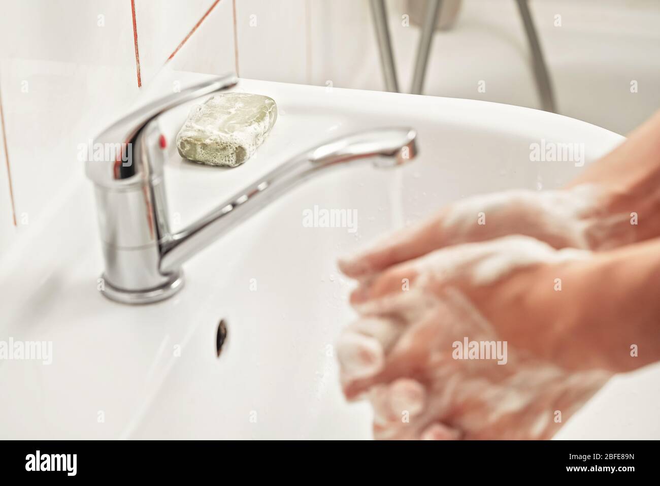 Young man washing hands under tap water with soap, focus on soapbar in ...