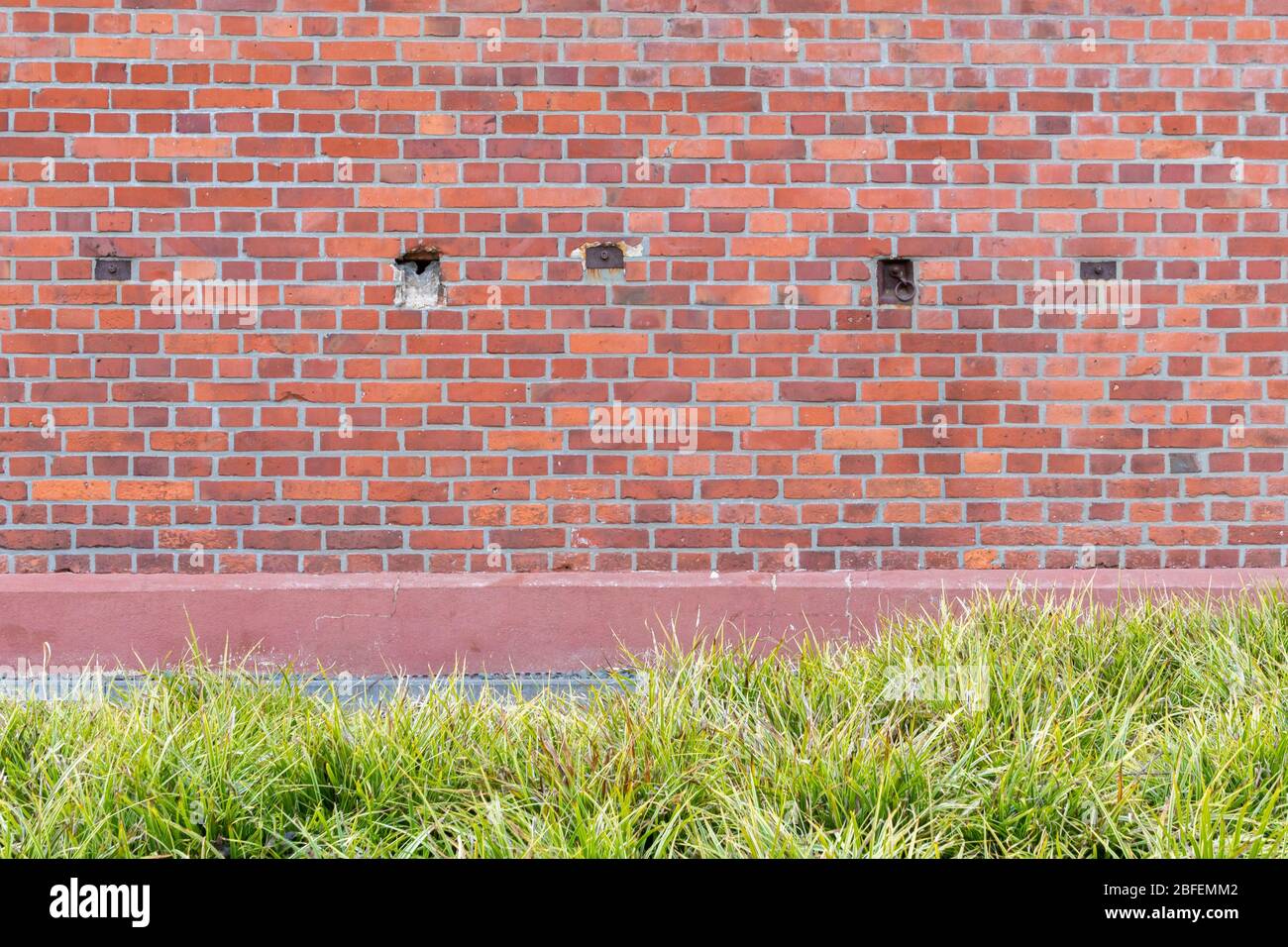 Old red brick wall of factory behind grass meadow Stock Photo - Alamy