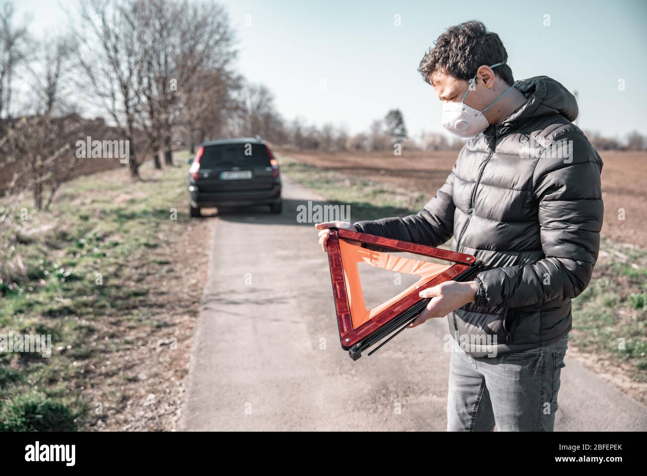 young man installs an orange warning triangle on the road in front of a ...
