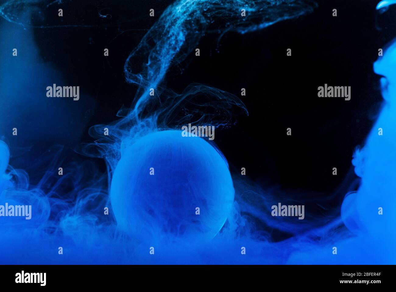Glass ball with blue paint splash underwater and on a black backgorund ...