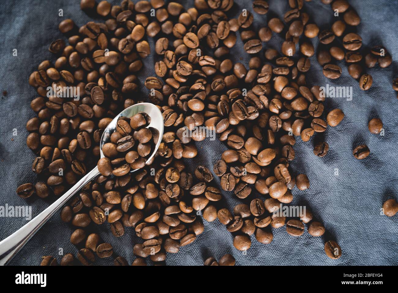 Dark roast coffee beans scattered on dark background with spoon. Coffee ...