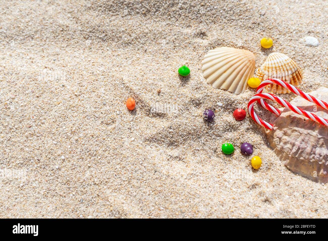 candy cane, seashells and colorful chocolate candies on the sandy beach ...