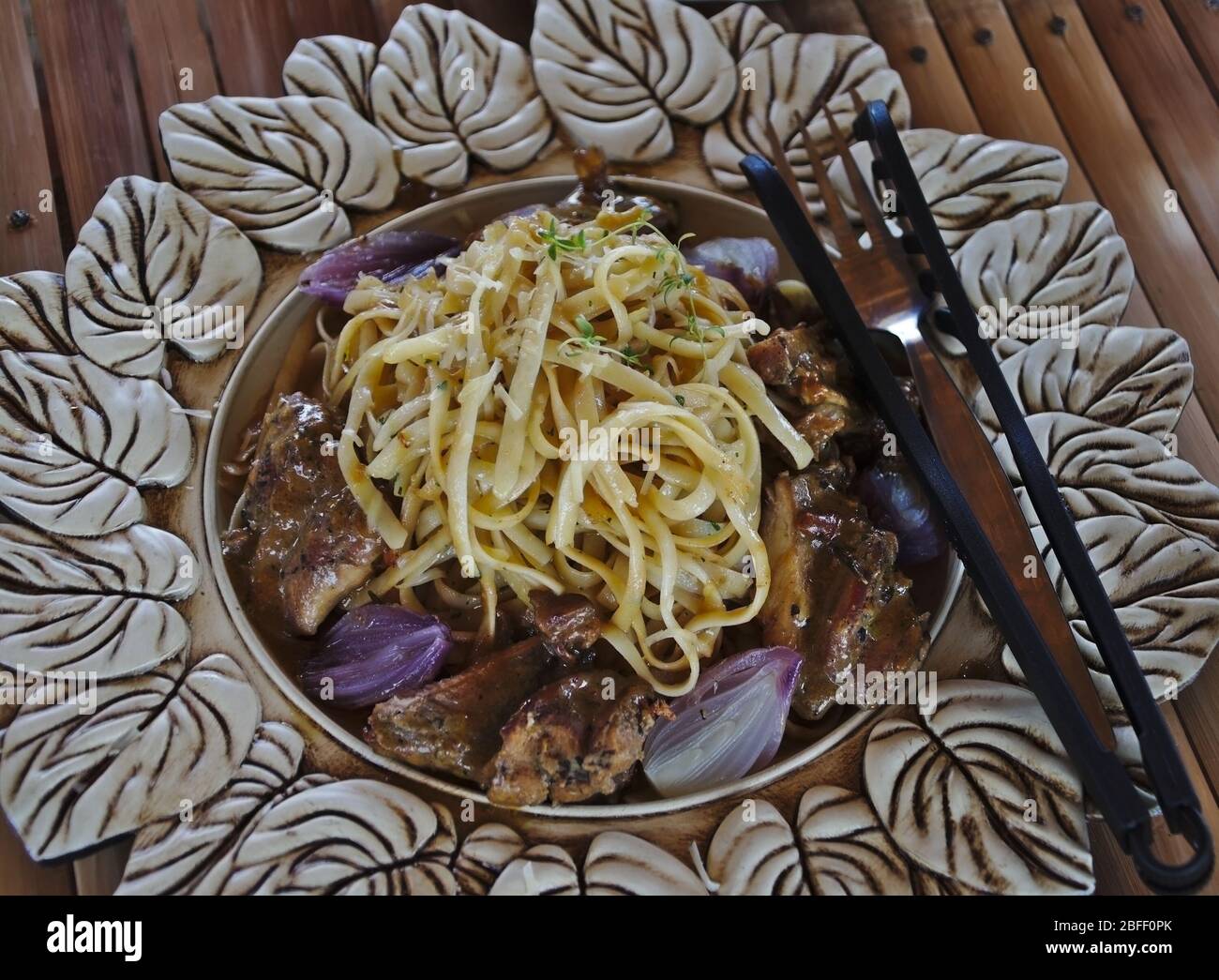 Cooked rabbit meat with pasta, onions, and other spices on a bamboo ...