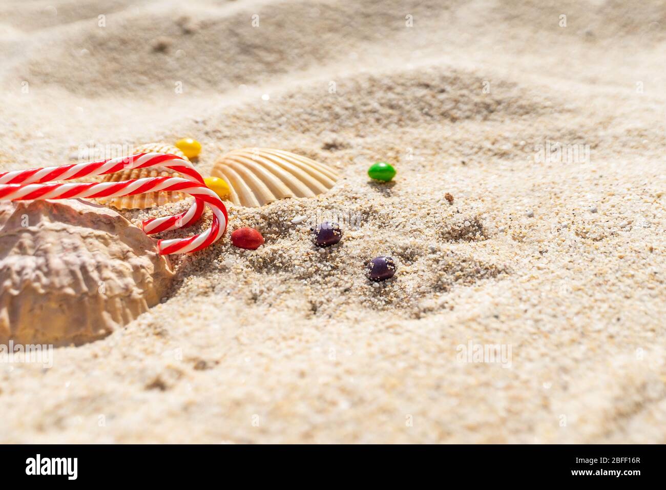 candy cane, seashells and colorful chocolate candies on the sandy beach ...