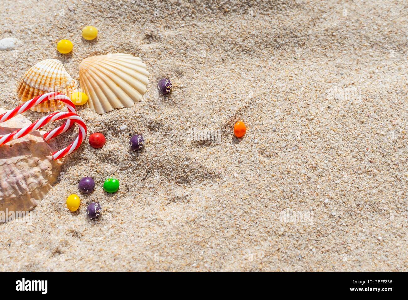 candy cane, seashells and colorful chocolate candies on the sandy beach ...