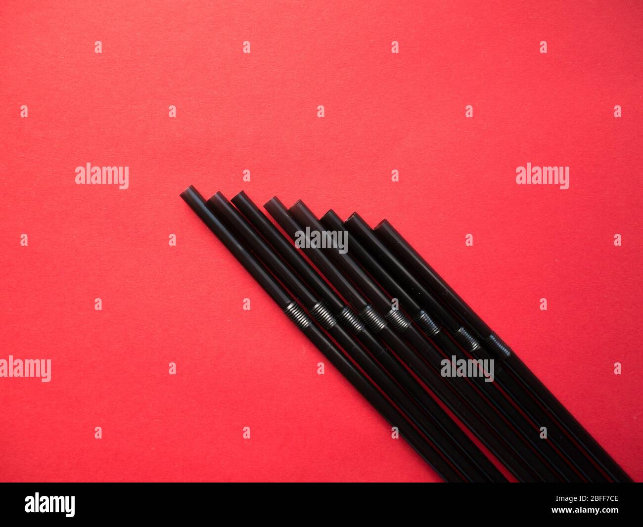Black plastic single use straws isolated on red background. Top view ...