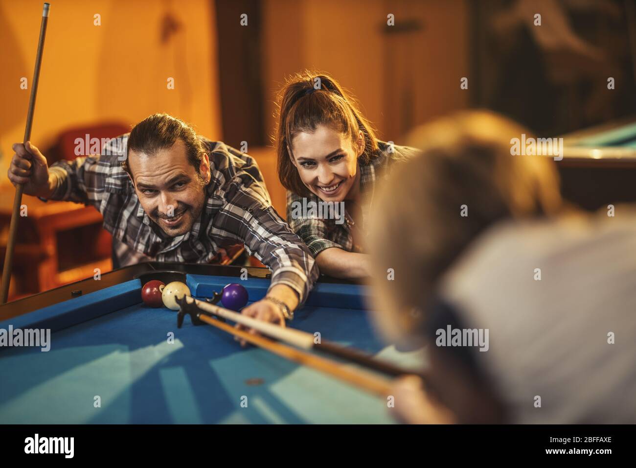 Group of a smiling cheerful friends are playing billiards in bar after ...