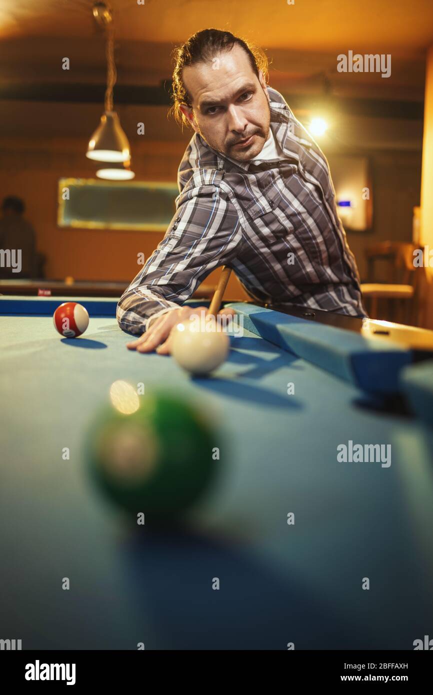 Concentrated middle aged man while playing billiards in billiard club ...