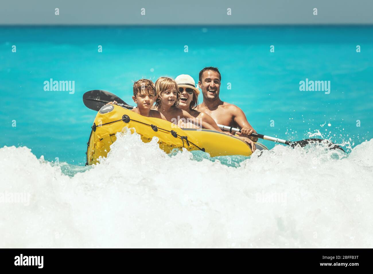 Happy family is enjoying a ride in rubber kayak and waves are splashing ...
