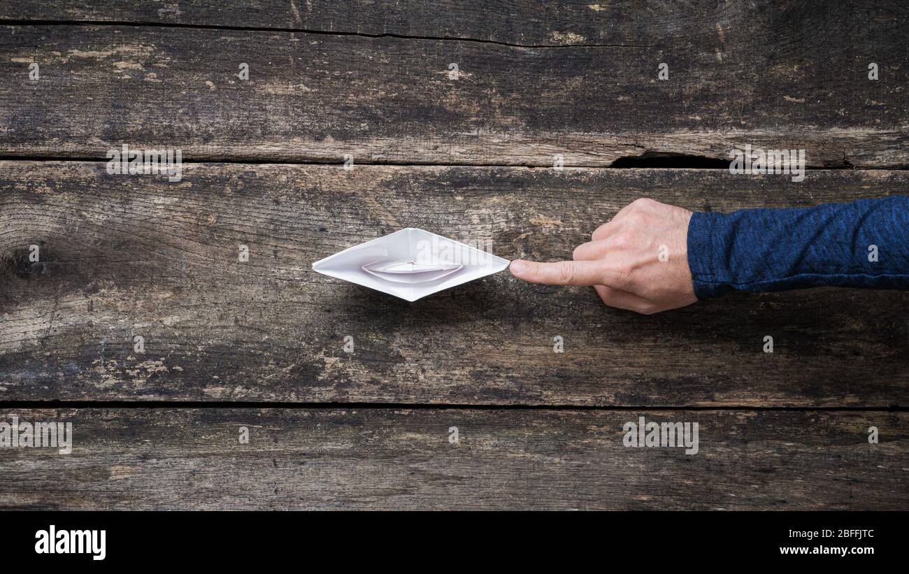 Top view of male finger pushing forward a paper made origami boat in a ...