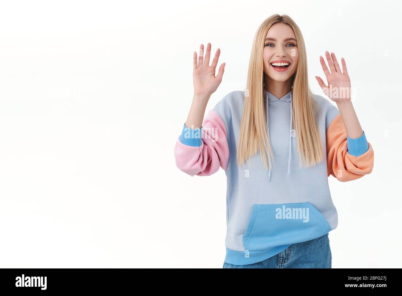 Happy good-looking blonde girl in hoodie, waving both hands in farewell ...