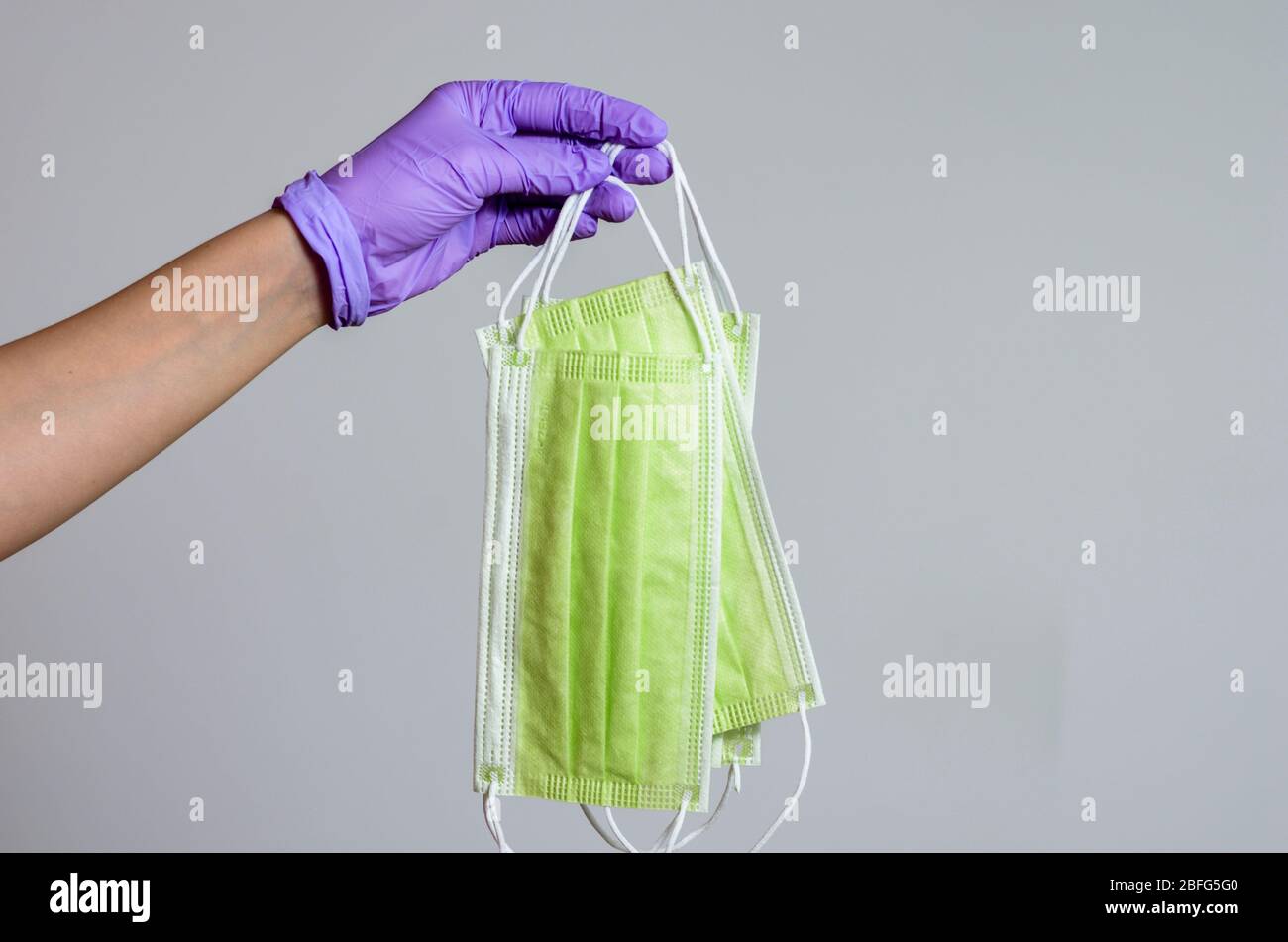 Woman's hand with surgical glove holding surgical face masks on a gray ...
