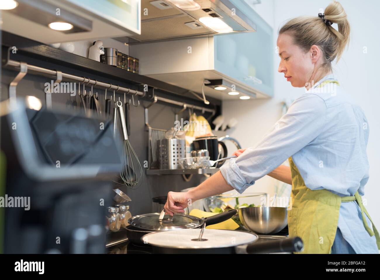 Stay at home housewife woman cooking in kitchen, stir frying dish in a ...