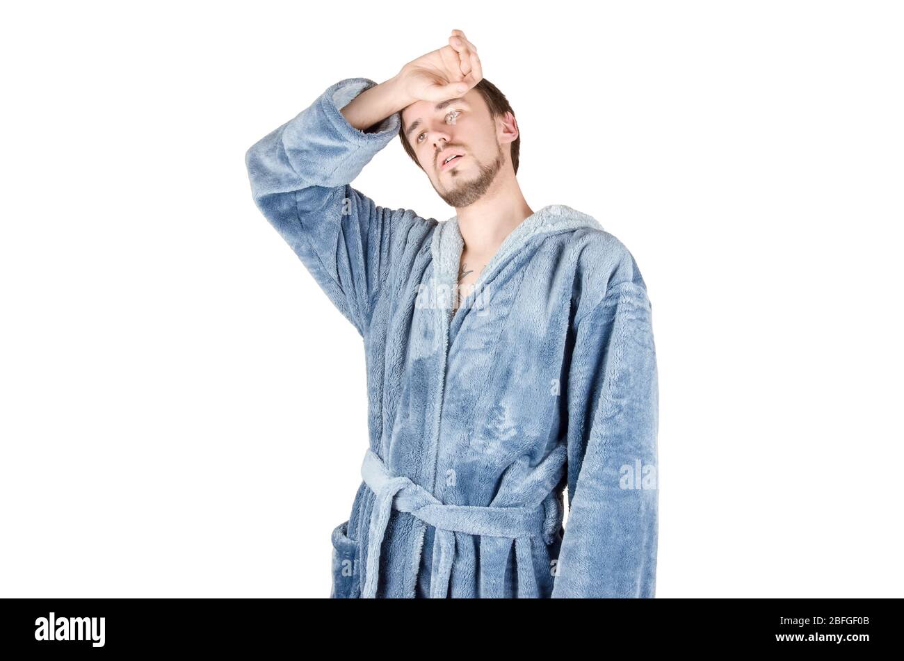 Portrait of young caucasian bearded man in blue bathrobe shows tired ...