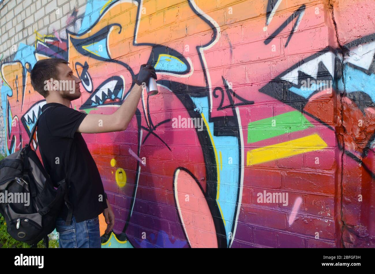Young graffiti artist with backpack and gas mask on his neck paints ...