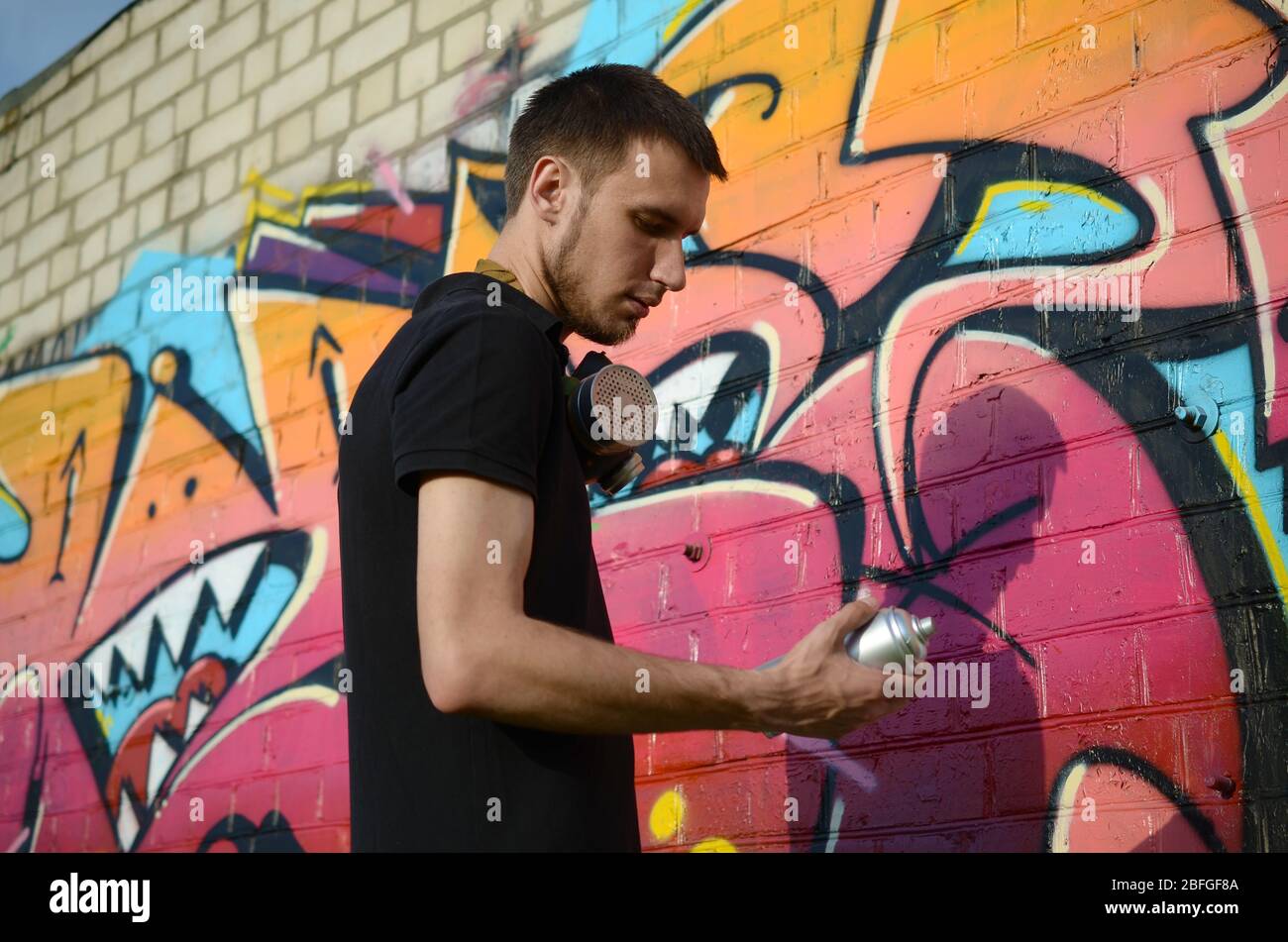 Young graffiti artist with backpack and gas mask on his neck paints ...