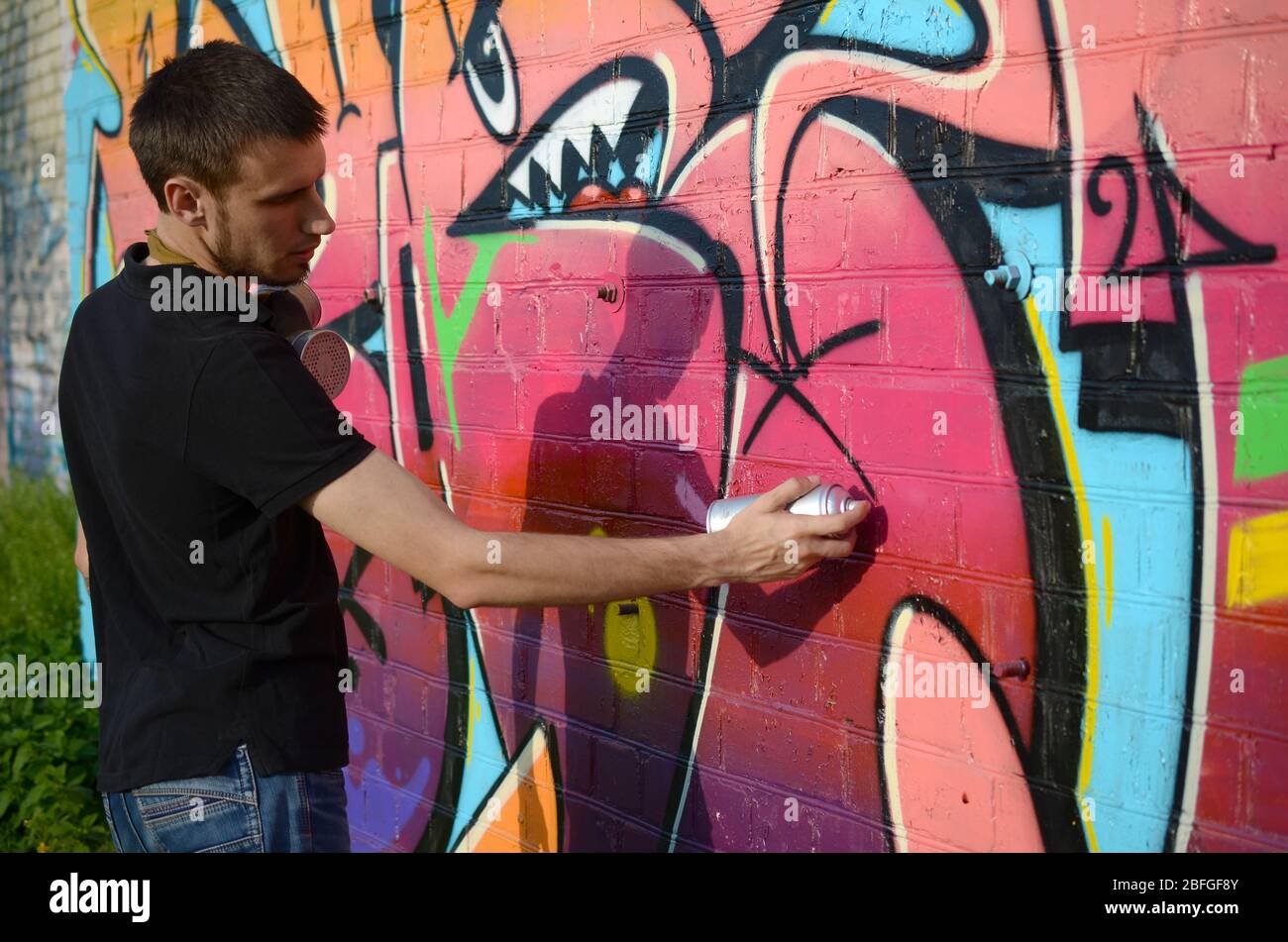 Young graffiti artist with backpack and gas mask on his neck paints ...