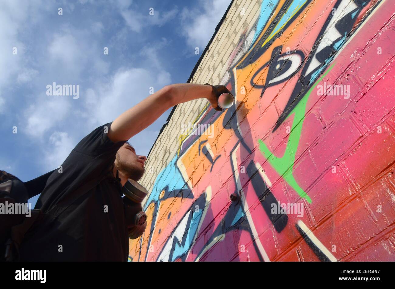 Young graffiti artist with backpack and gas mask on his neck paints ...
