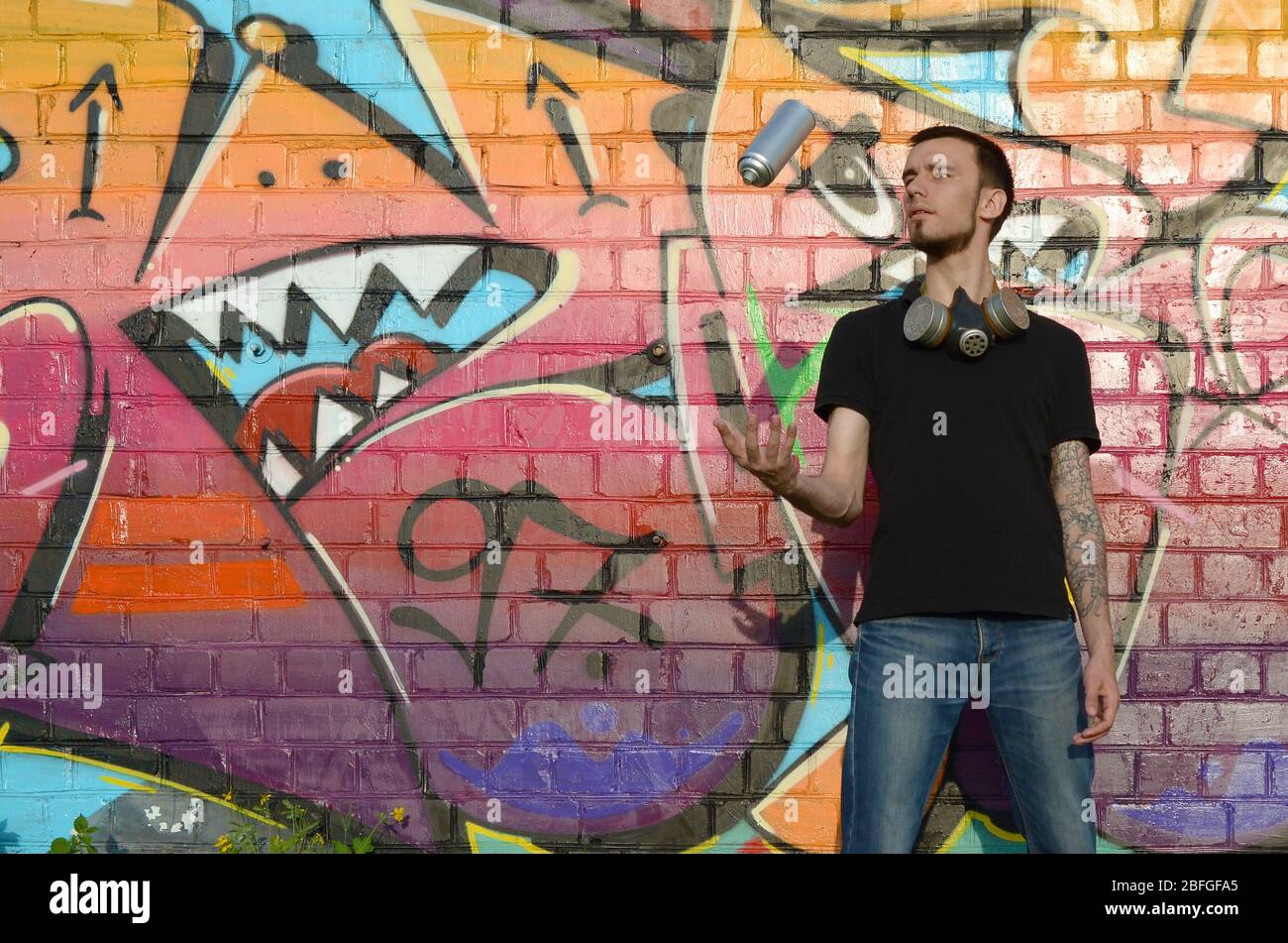 Young graffiti artist with gas mask on his neck throw his spray can ...