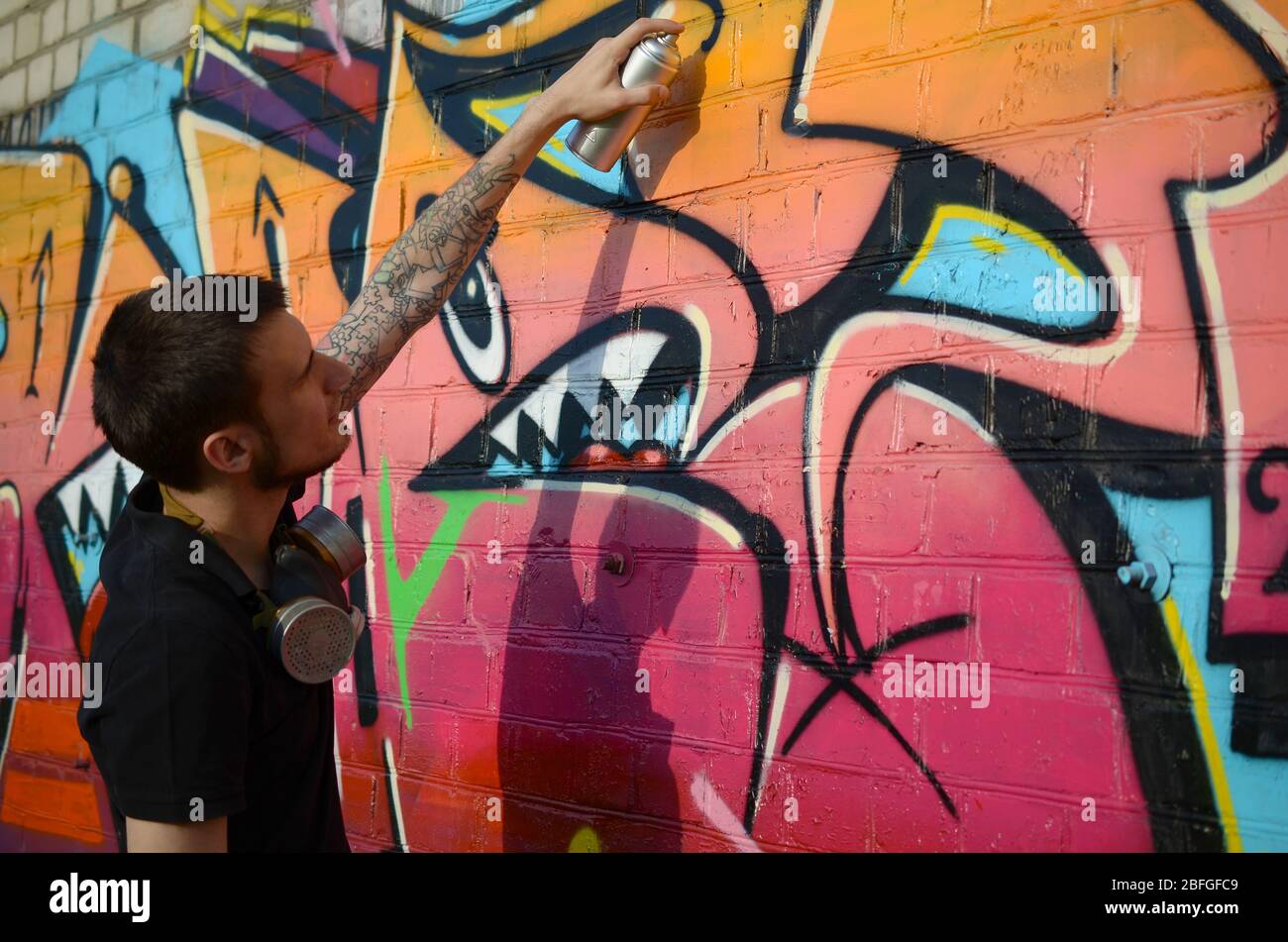 Young graffiti artist with backpack and gas mask on his neck paints ...