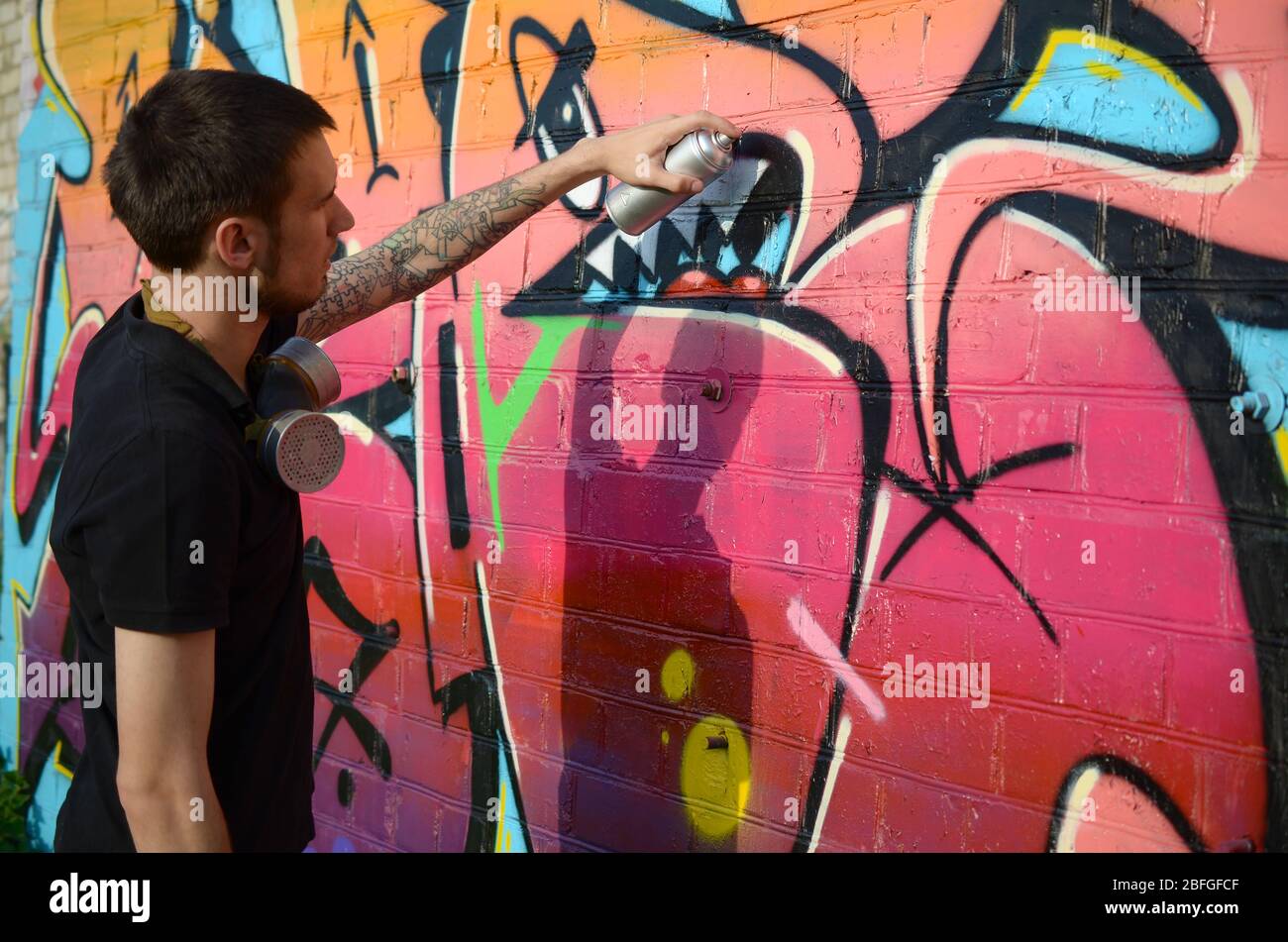 Young graffiti artist with backpack and gas mask on his neck paints ...