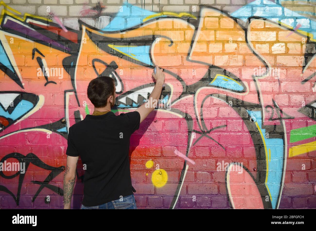 Young graffiti artist with backpack and gas mask on his neck paints ...