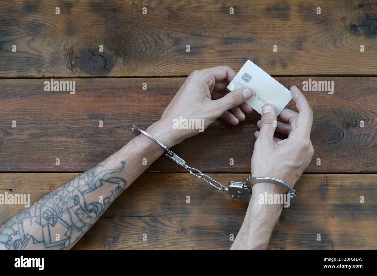 Cuffed hands of tattooed criminal suspect of carding holds fake credit ...