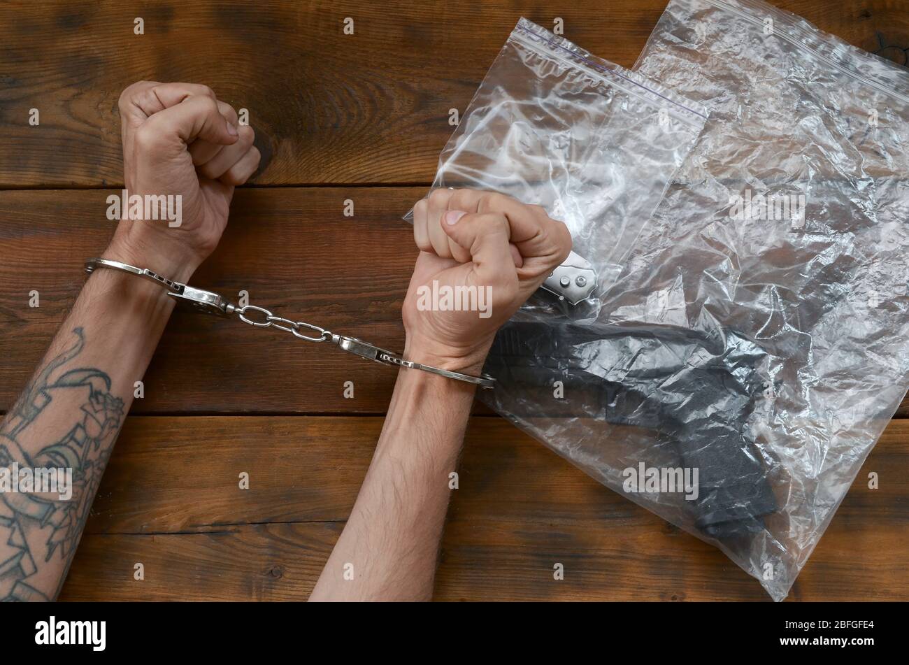 Handcuffed hands of criminal suspect on wooden table and crime scene ...