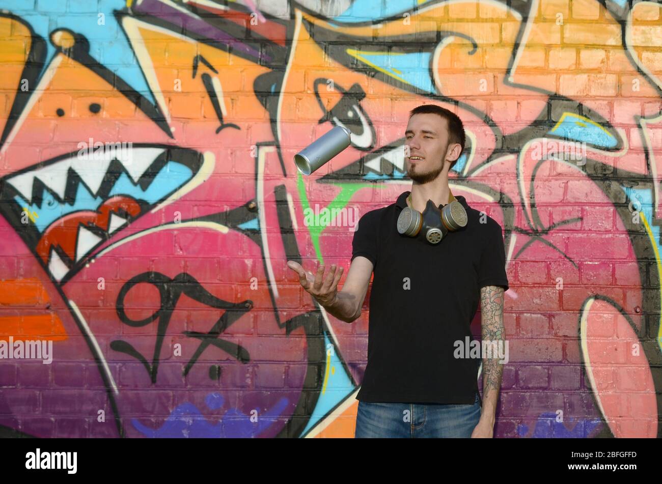 Young graffiti artist with gas mask on his neck throw his spray can ...