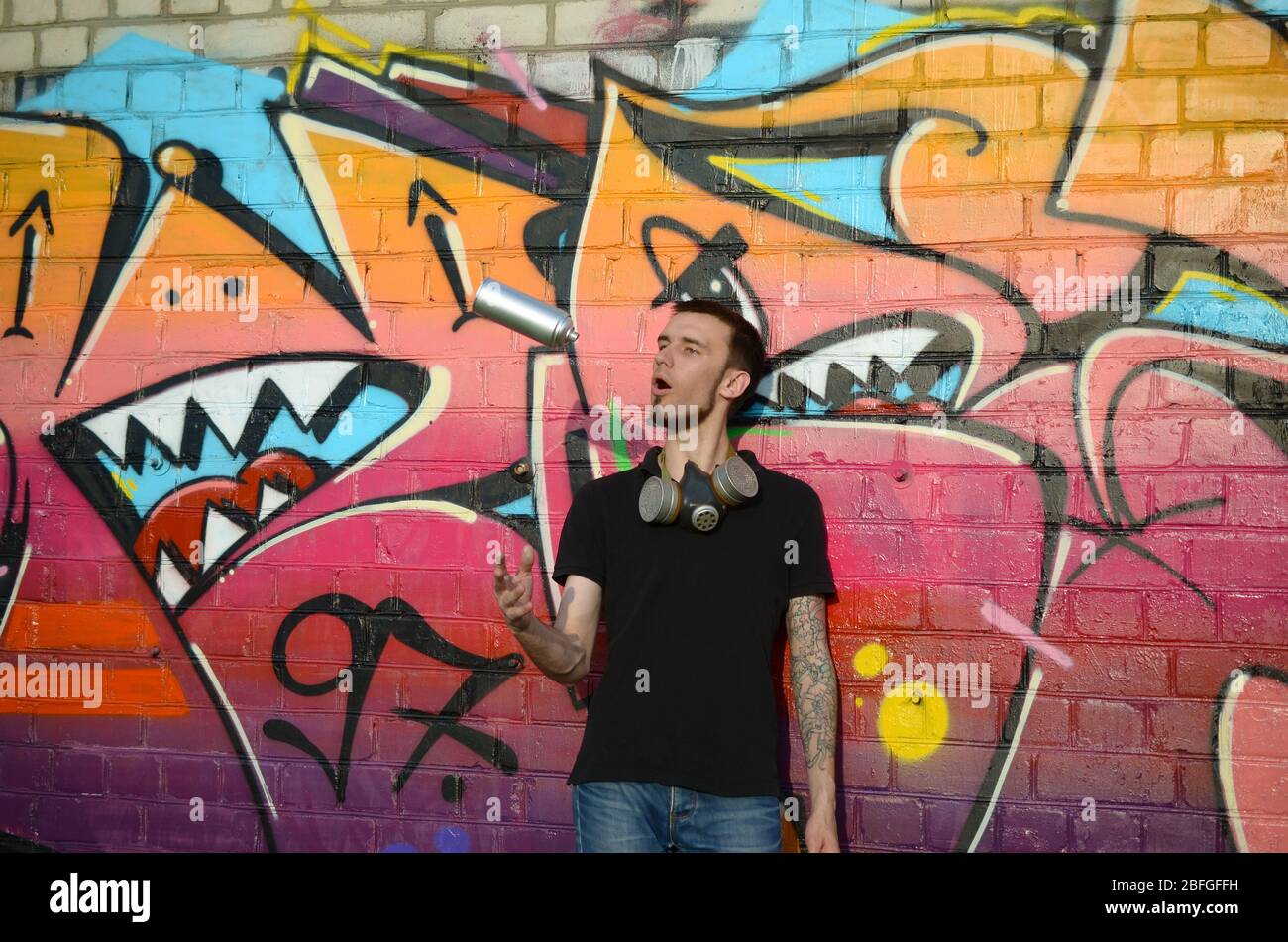 Young graffiti artist with gas mask on his neck throw his spray can ...