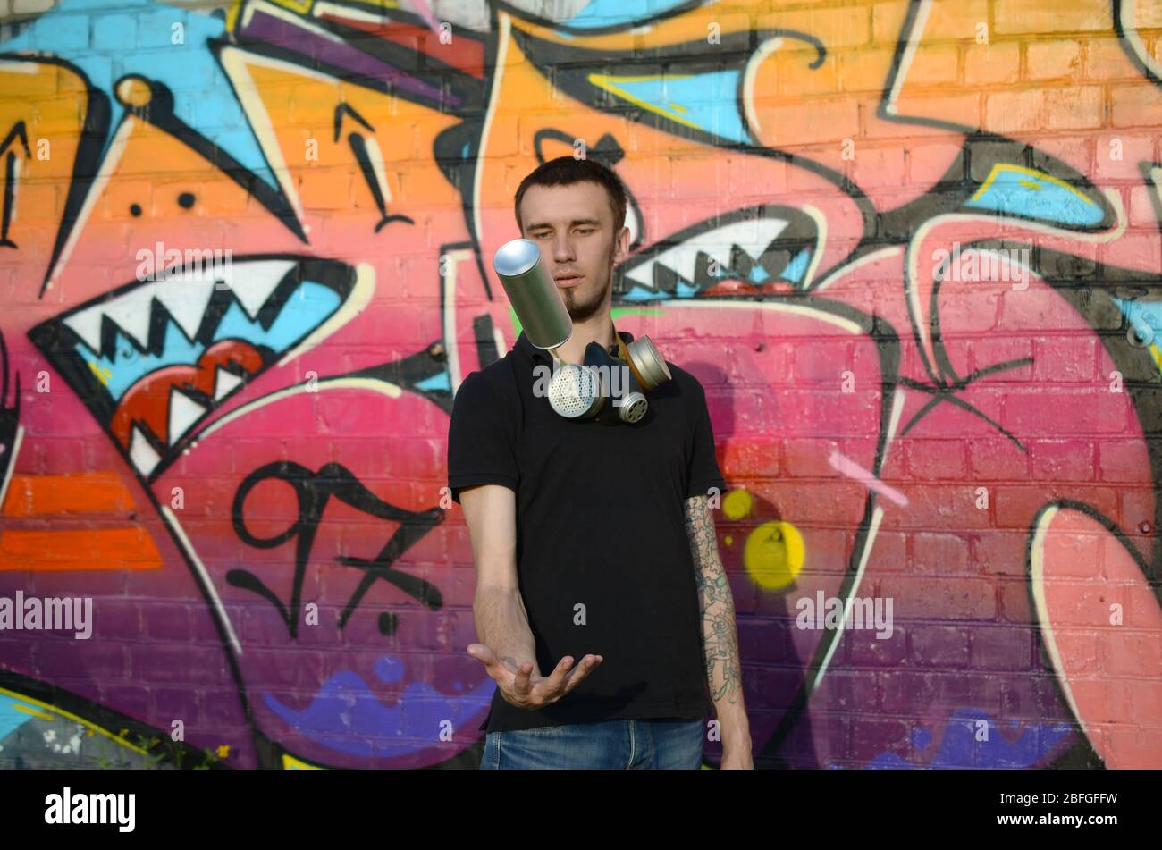 Young graffiti artist with gas mask on his neck throw his spray can ...