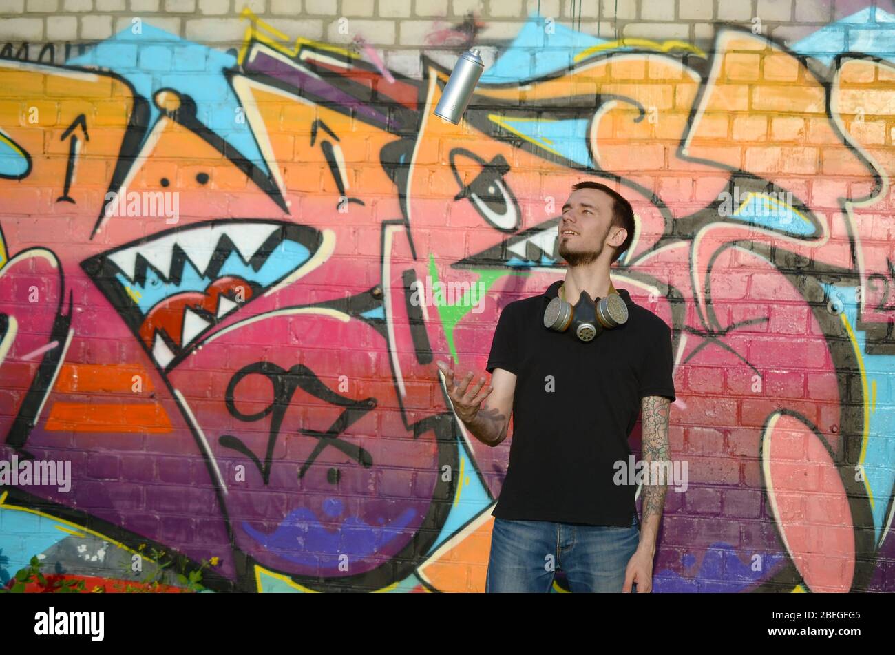 Young graffiti artist with gas mask on his neck throw his spray can ...