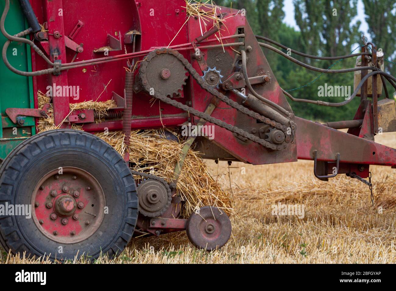 A tractor with a trailed bale making machine collects straw rolls in ...